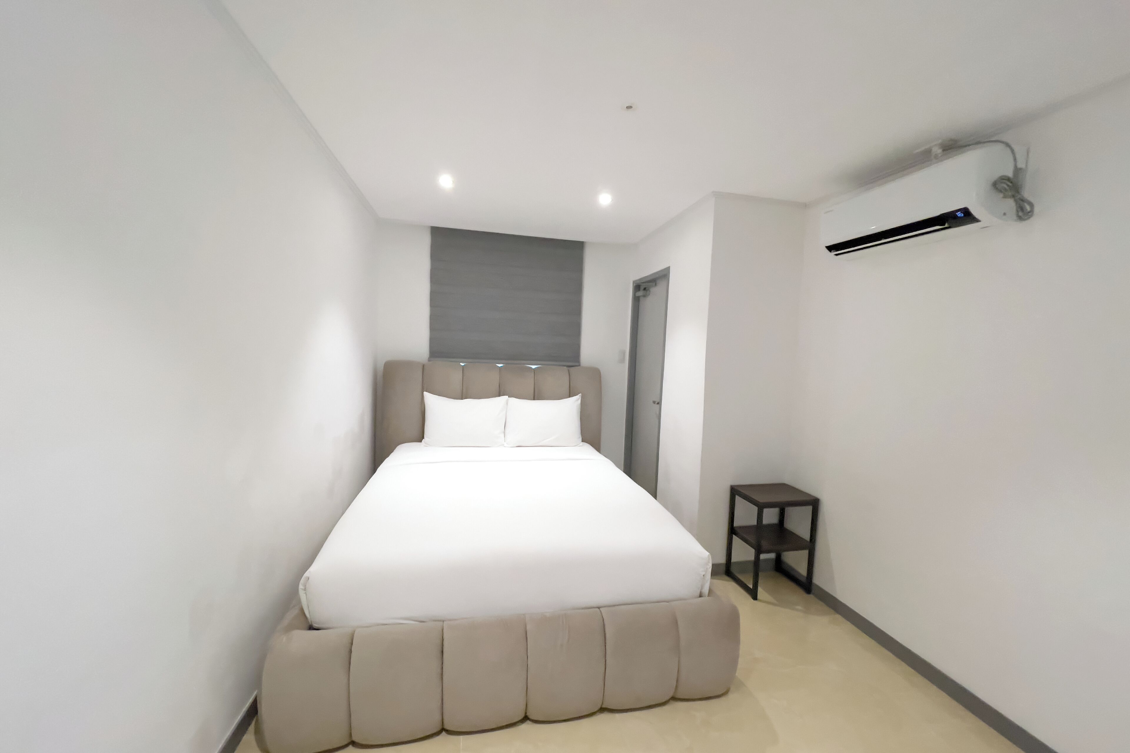 Quarto moderno com uma cama grande, uma mesa de cabeceira pequena e um aparelho de ar condicionado na parede.