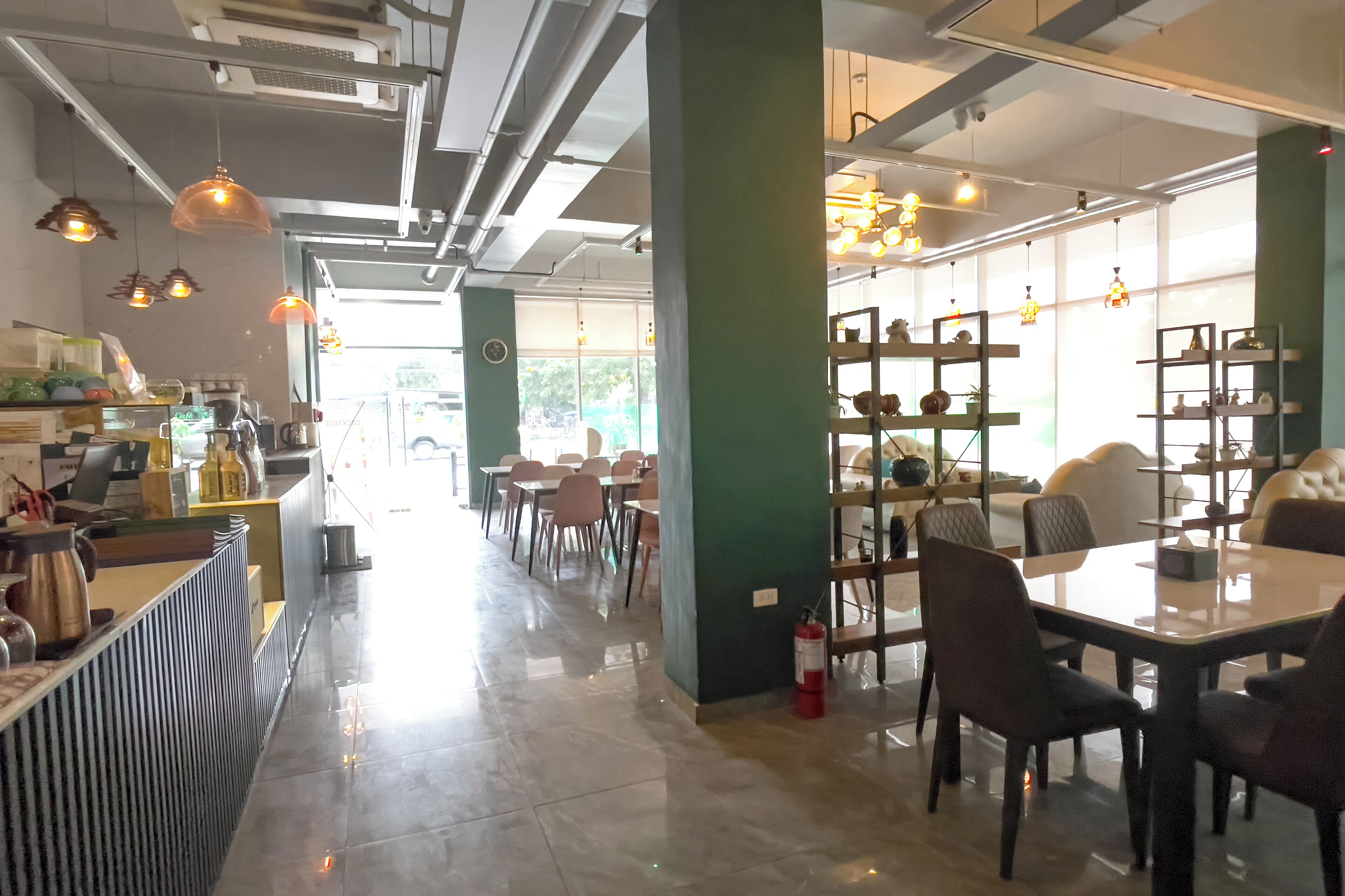Um café moderno com design limpo e minimalista, apresentando um balcão com diversos produtos, áreas de estar com mesas e cadeiras, e iluminação pendente.