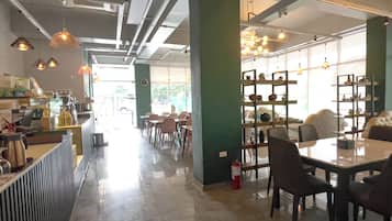 Um café moderno com design limpo e minimalista, apresentando um balcão com diversos produtos, áreas de estar com mesas e cadeiras, e iluminação pendente.