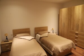 Quarto com duas camas, cabeceiras de madeira, abajures e um guarda-roupa espaçoso.