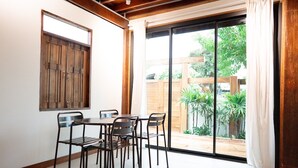 Uma área de refeições com mesa, cadeiras, um armário de madeira e uma porta de vidro deslizante que dá para um jardim.