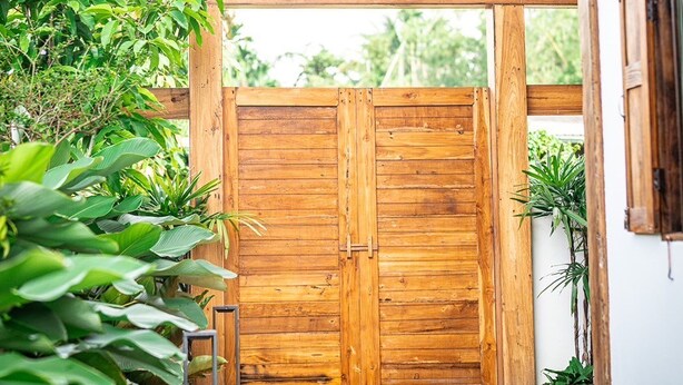 Um portão de madeira que dá para uma casa com fachada branca e um pequeno jardim.