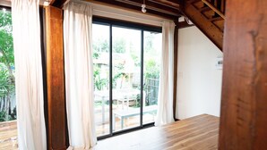 Quarto com piso de madeira e grandes portas de vidro deslizantes que dão para área externa com mesa e cadeiras.