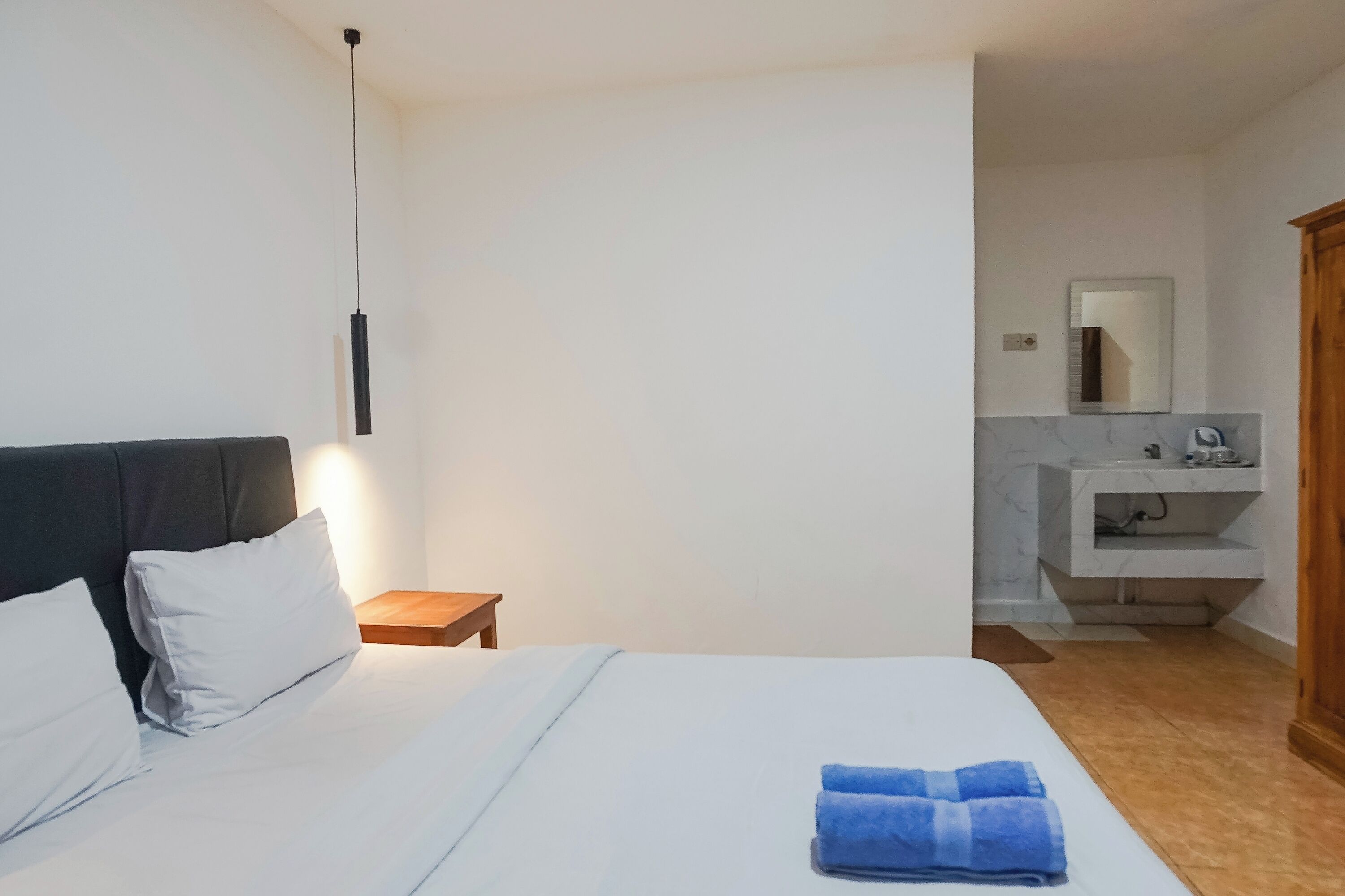 Quarto de hotel com cama, mesa de cabeceira, banheiro com pia e espelho, e guarda-roupa de madeira.