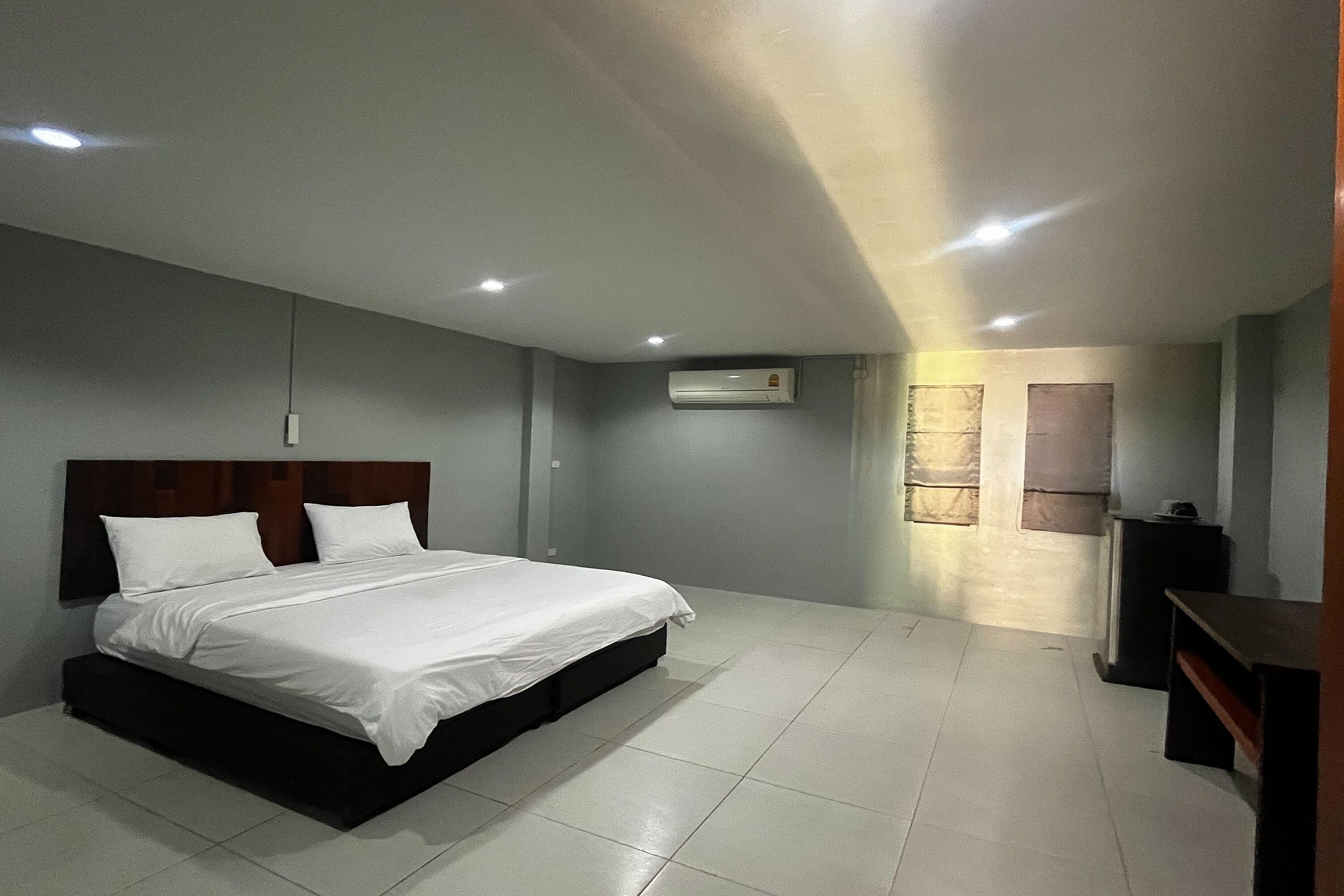 Quarto de hotel moderno com uma cama grande, cabeceira de madeira, aparelho de ar condicionado e uma pequena mesa.