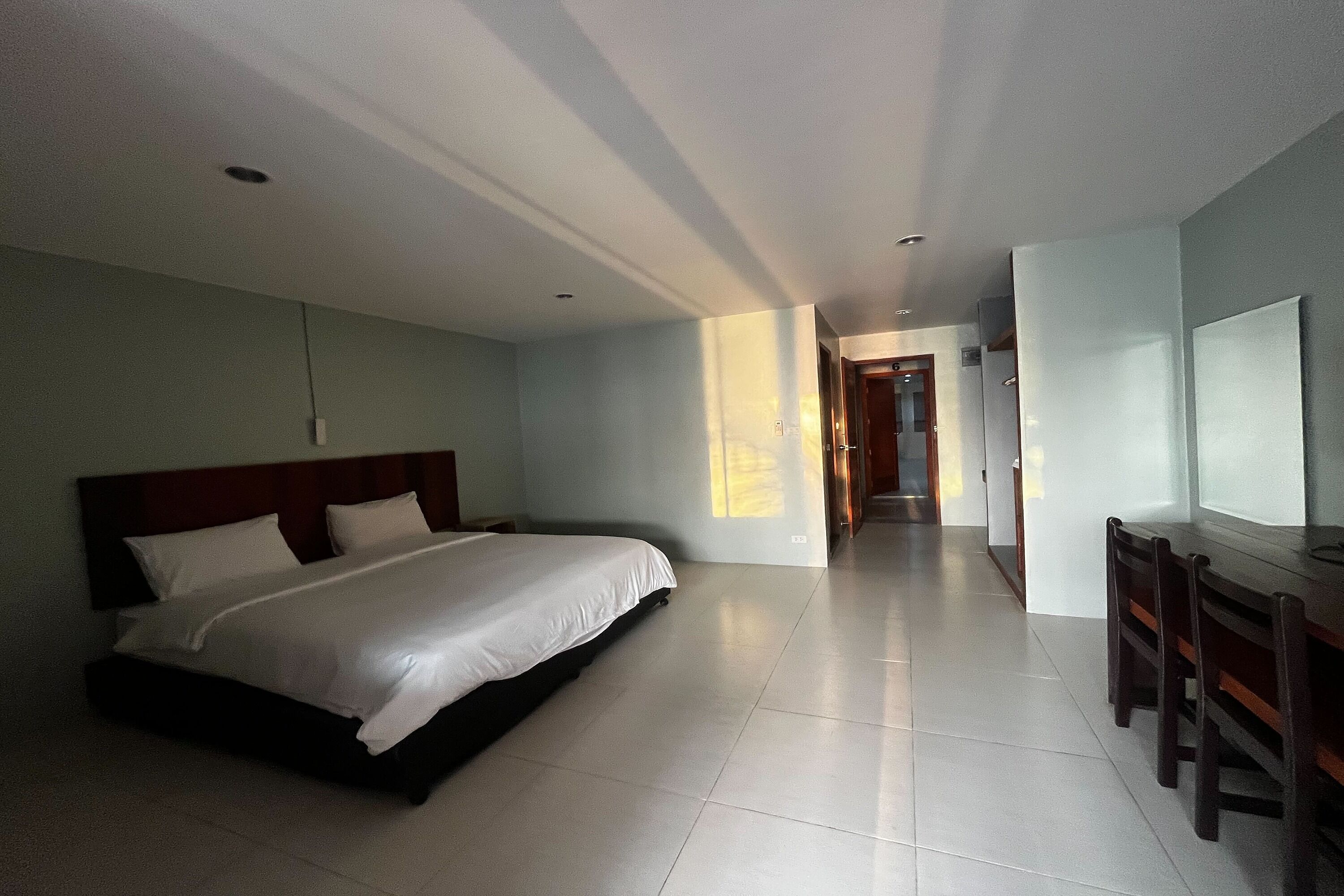 Quarto de hotel com uma cama grande, uma escrivaninha e uma cadeira. Há uma porta que dá para outro quarto.