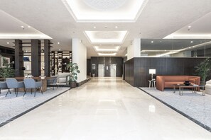 Um hall amplo com piso de mármore polido, balcão de recepção, área de estar e escada moderna.