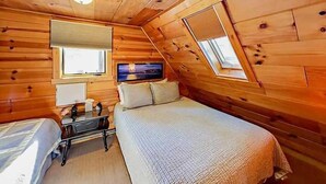 Um quarto de cabana de madeira aconchegante, com uma cama, uma escrivaninha e uma televisão.