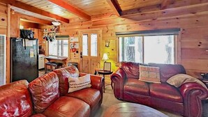 Interior de cabana com decoração em madeira, área de jantar e sala de estar com sofás de couro.
