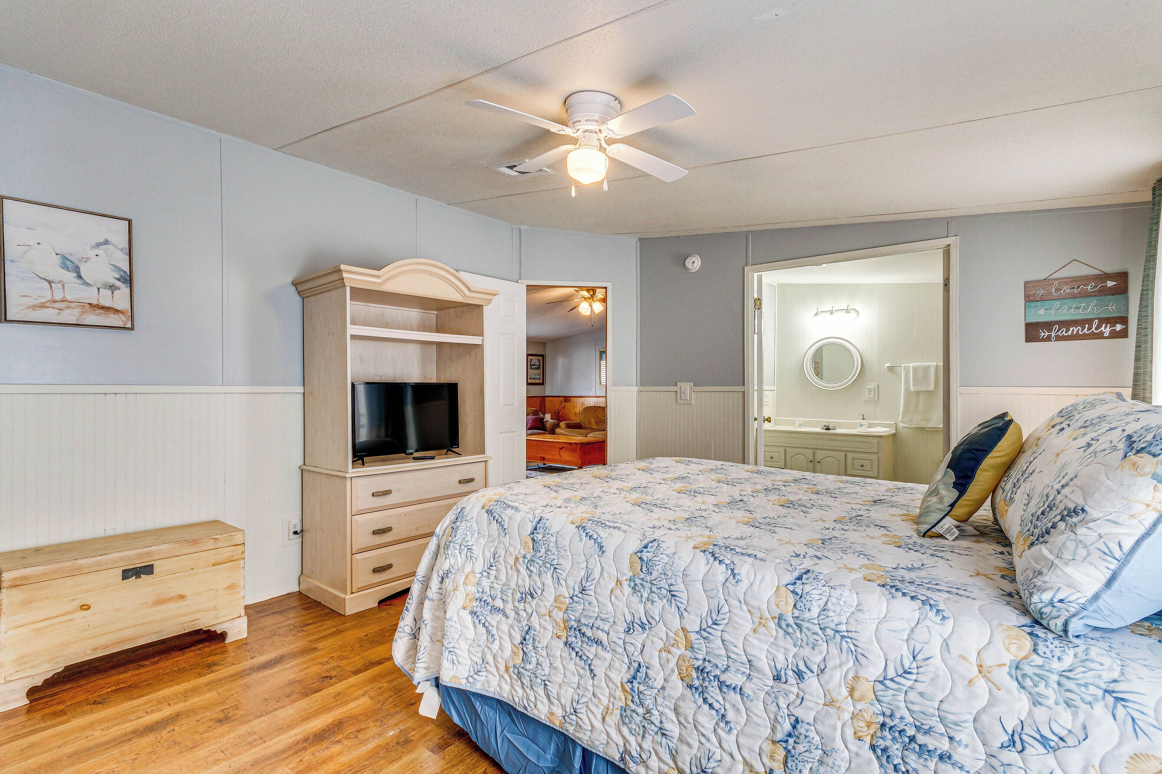 Quarto com cama, televisão, ventoinha no teto e cómoda de madeira.