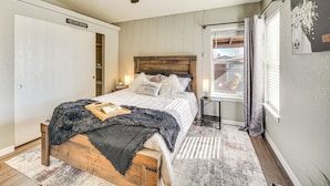 Quarto com cama de madeira, ventoinha no teto, janela com cortinas e mesa de cabeceira com abajur.