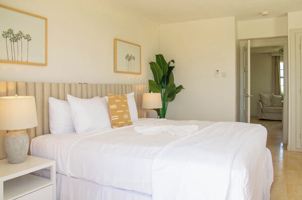 Cama bem arrumada com roupa de cama branca, duas luminárias de cabeceira e uma grande planta verde ao lado da cama.