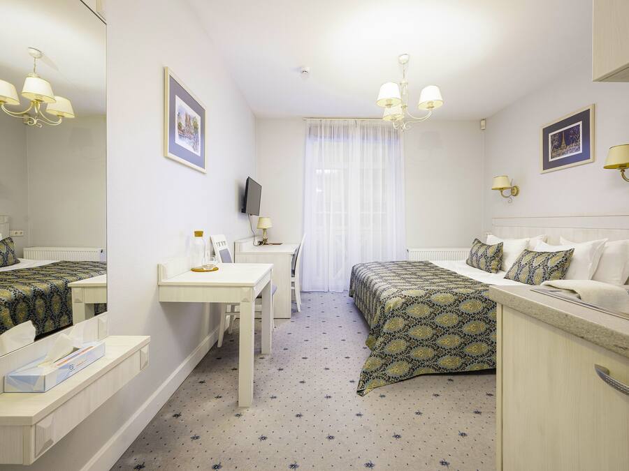 Quarto de hotel com cama, escrivaninha, cadeira, televisão e janela com cortinas.