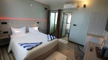 Quarto de hotel com cama, mesa de cabeceira e um pequeno espaço de estar com uma cadeira e uma mesa.