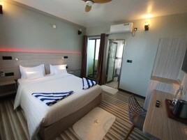 Quarto de hotel com cama, mesa de cabeceira e um pequeno espaço de estar com uma cadeira e uma mesa.