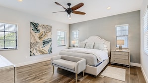 Quarto com cama, um banquinho, mesa de cabeceira e ventilador de teto.