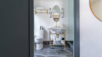 Casa de banho com sanita branca, toucador dourado com espelho e chão com padrão herringbone.