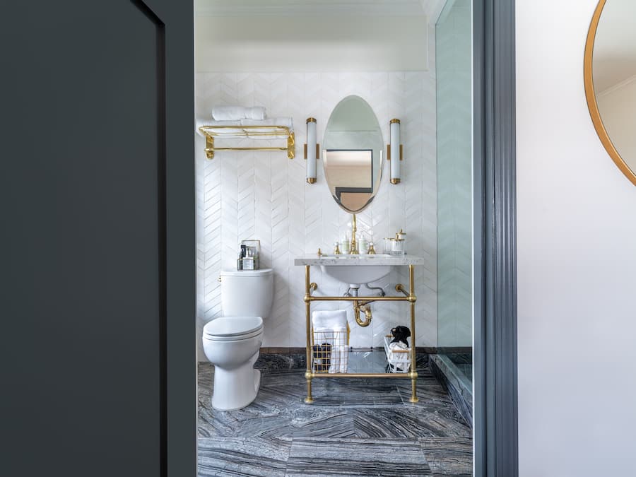 Casa de banho com sanita branca, toucador dourado com espelho e chão com padrão herringbone.