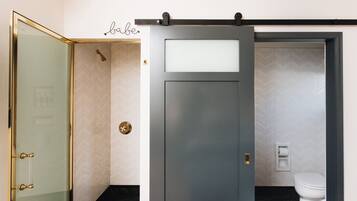 Casa de banho com chuveiro, sanita e porta com painel leitoso.