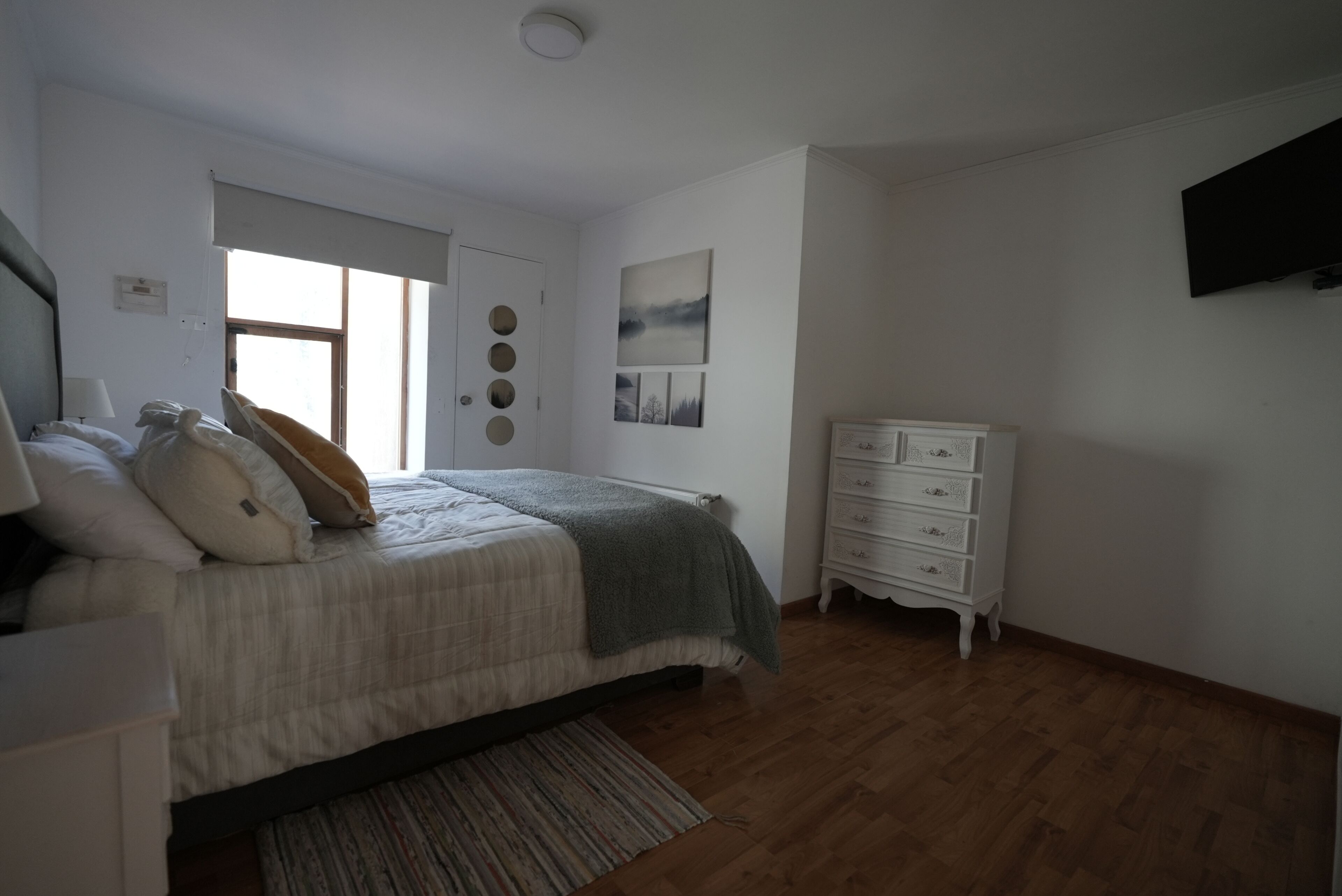 Quarto com cama, cómoda, janela e televisão fixada na parede.