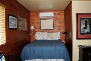 Quarto com painéis de madeira, uma cama, quadros, ar condicionado e uma luminária.