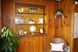 Interior em madeira com uma estante exibindo um relógio, plantas, um globo e uma moldura.