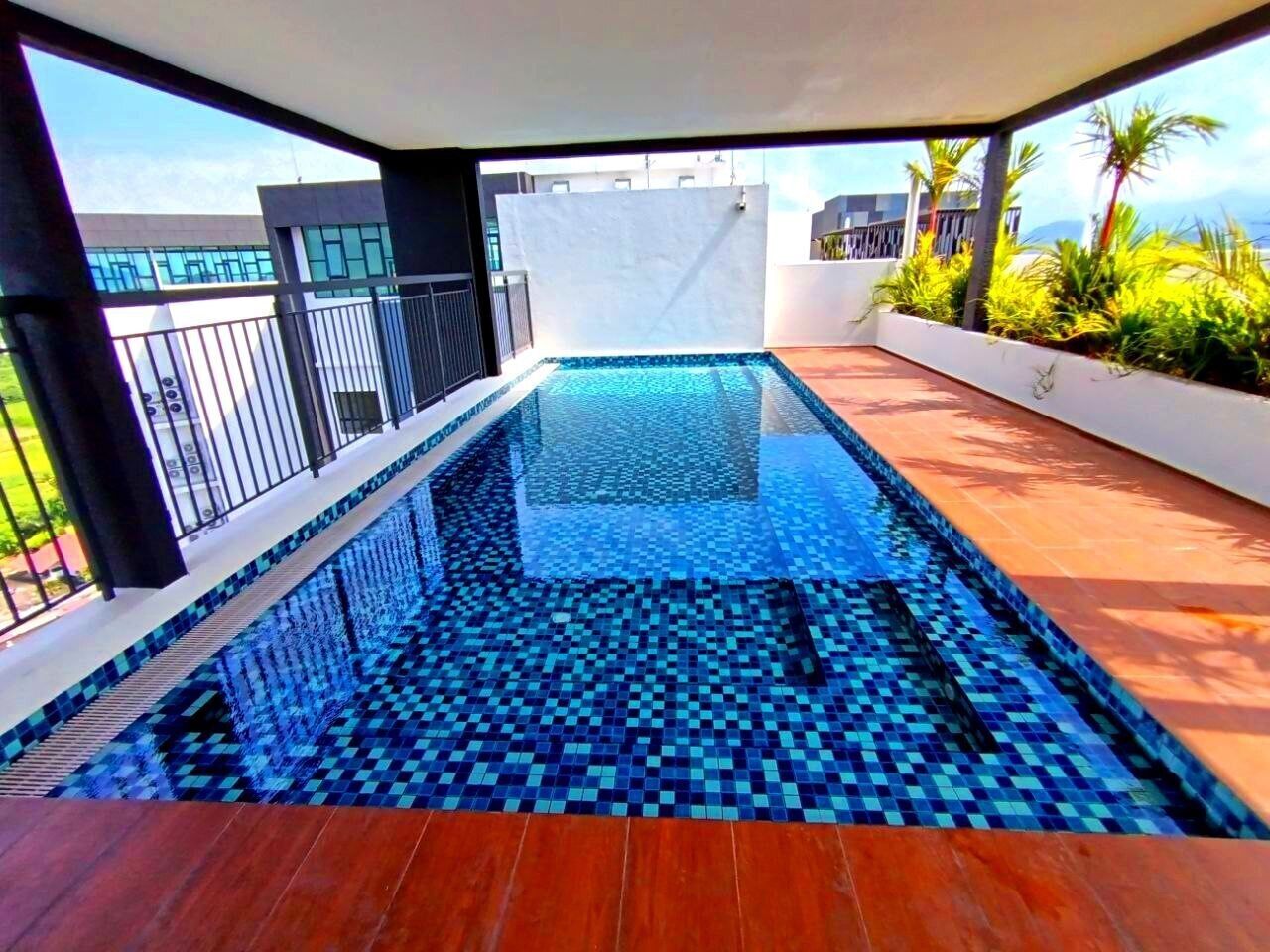 Piscina interior retangular com azulejos de mosaico azul e preto, rodeada por um deck de madeira e uma parede branca.