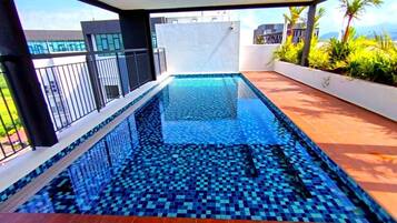 Piscina interior retangular com azulejos de mosaico azul e preto, rodeada por um deck de madeira e uma parede branca.