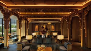 Um hall luxuoso com colunas ornamentadas, um sofá central e uma mesa de centro.