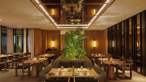 Uma sala de jantar moderna com disposição central de assentos, uma planta grande e teto alto com iluminação embutida.