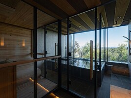 Um interior moderno com paredes de vidro, vigas de madeira e vista para o verde.