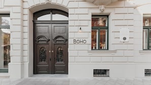 Fachada de edifício com entrada por portas duplas, placa com a inscrição "BOHO" e uma placa com texto.