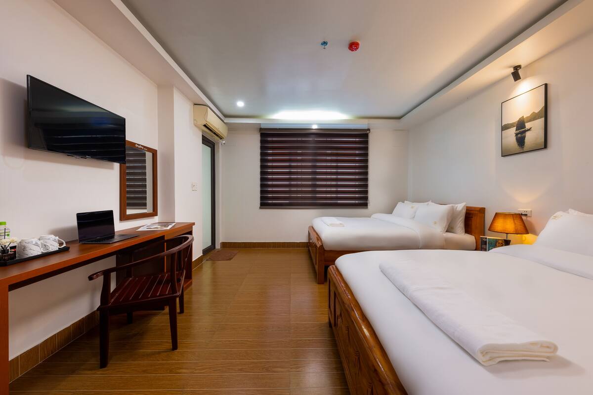 Quarto de hotel com secretária, duas camas, televisão e janela com persianas.