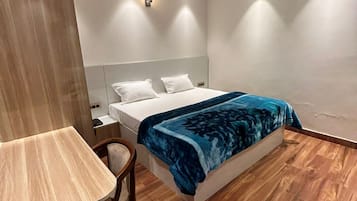 Quarto de hotel com cama, piso de madeira, ventilador de teto e mesa de cabeceira.