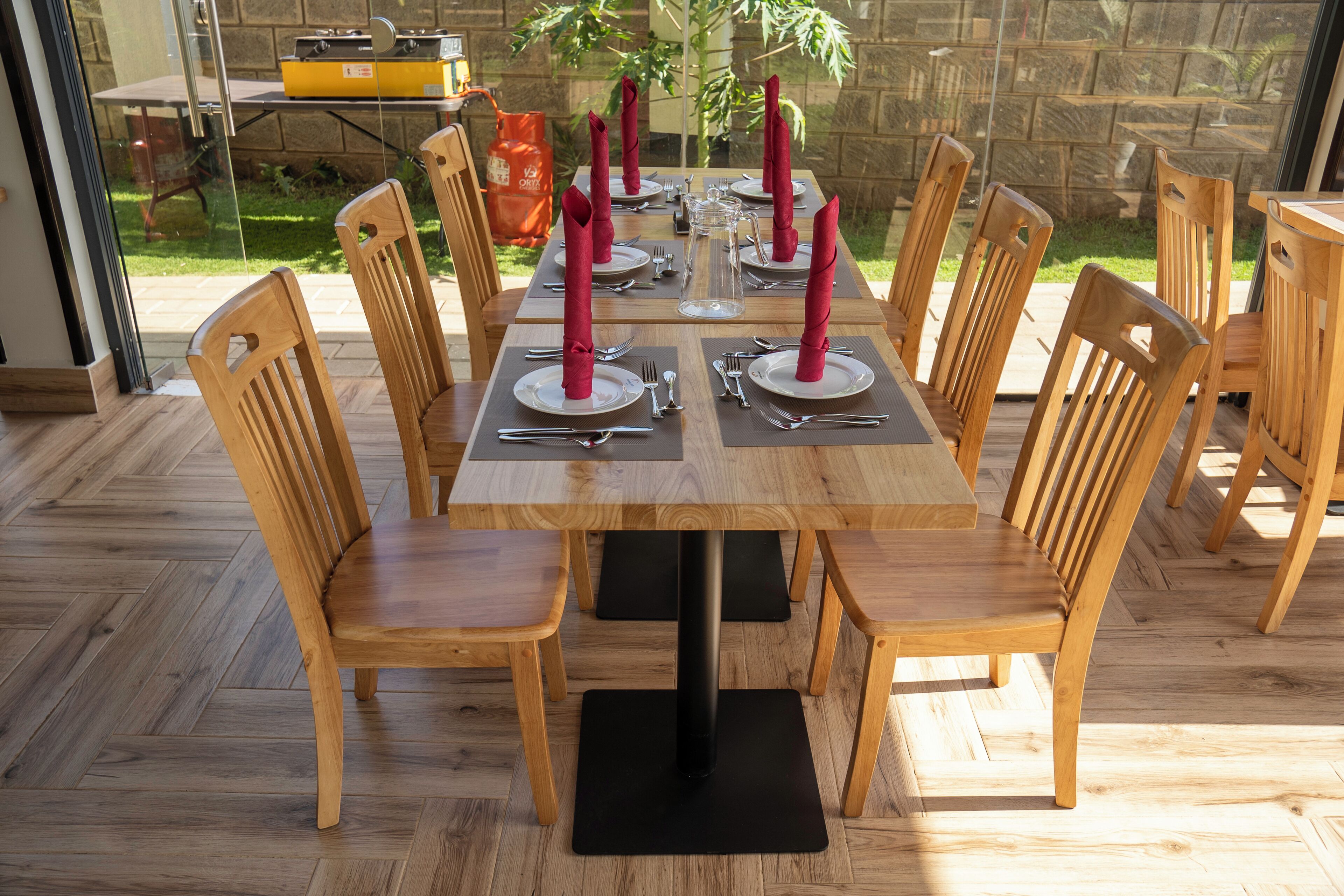 Mesa de jantar de madeira para seis pessoas, com cadeiras combinando, base preta e guardanapos vermelhos.