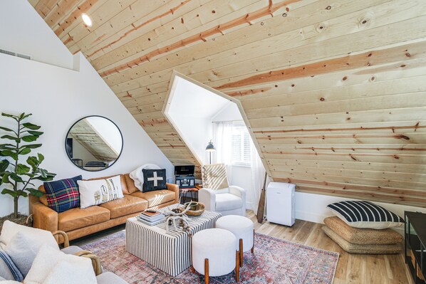 Um quarto acolhedor no estilo loft, com teto inclinado, espelho redondo, sofá de couro, mesa de centro e poltrona branca.