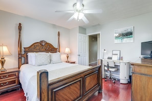 Quarto com cama de madeira, abajures, escrivaninha com cadeira, ventilador de teto e porta que dá para outro cômodo.