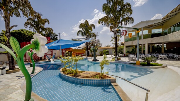Uma área de piscina com piso de azulejos, uma escultura de palmeira e mobiliário para área externa.