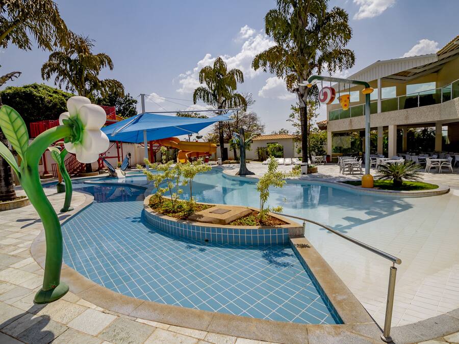Uma área de piscina com piso de azulejos, uma escultura de palmeira e mobiliário para área externa.