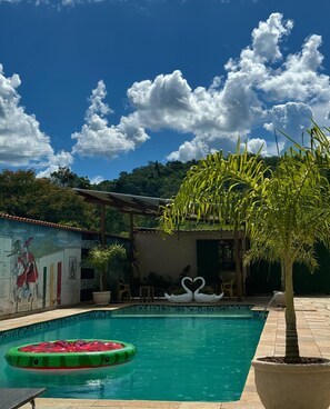 Piscina com mural, pérgola e uma árvore.