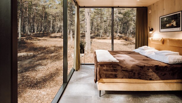 Quarto com cama grande, vista para uma floresta e design moderno.