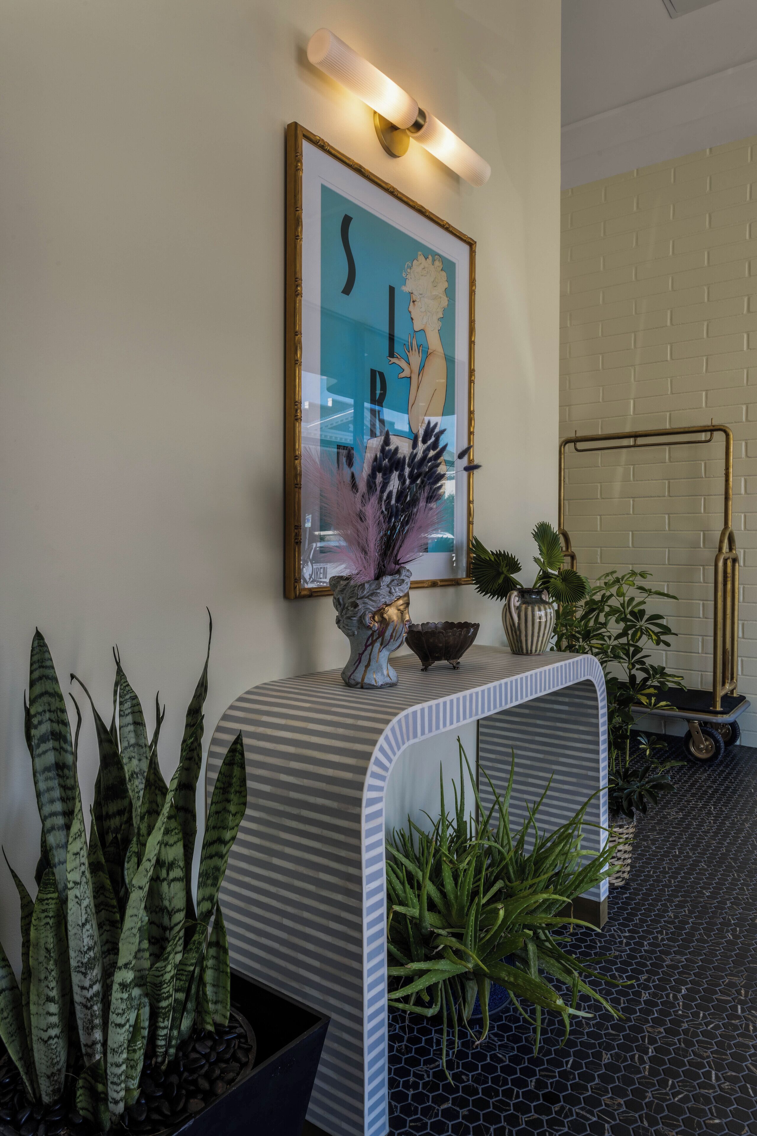 Uma área de recepção com uma obra de arte emoldurada, uma mesa consola com plantas e um espelho decorativo.