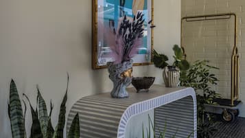 Uma área de recepção com uma obra de arte emoldurada, uma mesa consola com plantas e um espelho decorativo.