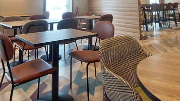 Uma sala de jantar moderna com várias mesas e cadeiras, um piso estampado e uma janela grande que permite entrada de luz natural.