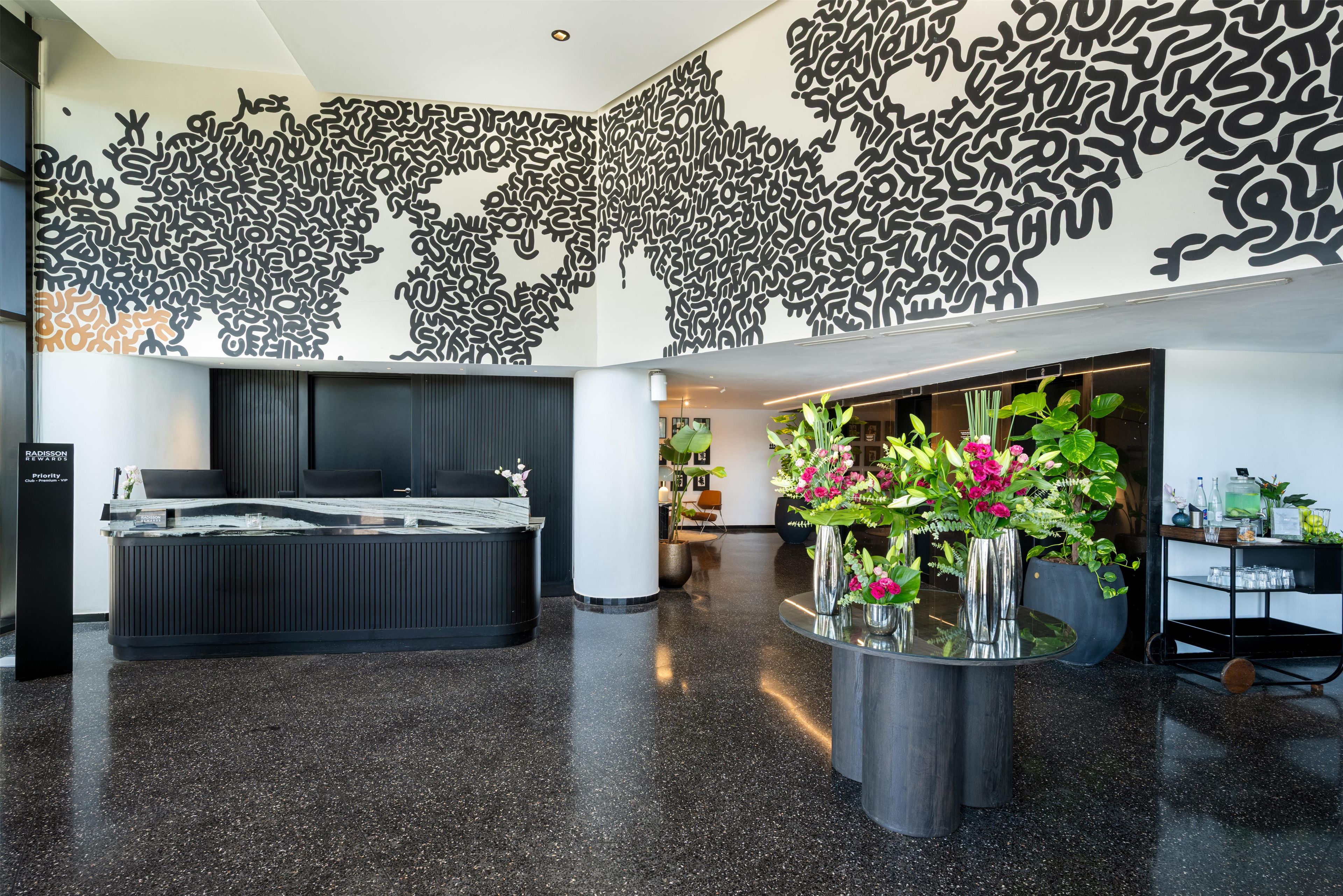 Um lobby moderno com balcão de recepção, um grande mural abstrato na parede e um arranjo floral central.