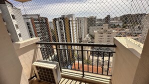 Uma varanda com grade de arame, com vista para um horizonte urbano com diversos edifícios.