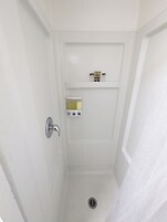 Um chuveiro interno pequeno e branco, com chuveiro, dosador de sabonete e ralo.