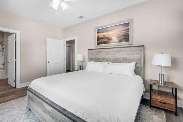 Quarto com cama grande, cabeceira de madeira, mesa de cabeceira com abajur e um quadro na parede.