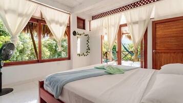 Quarto com cama, janela, ventilador e vista para o verde lá fora.