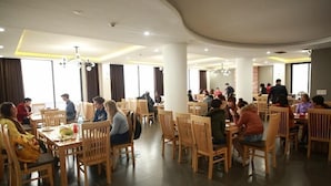 Uma sala de jantar ampla com mesas e cadeiras de madeira, janelas grandes e um design moderno no teto.